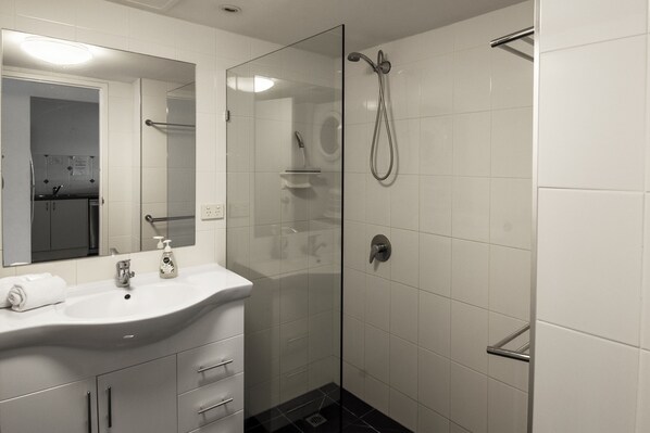 Uma casa de banho moderna com chuveiro em cabine de vidro, lavatório branco com espelho e chão em mosaico preto.