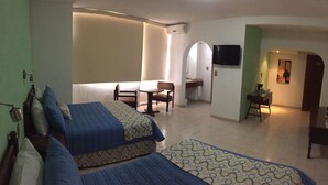 Quarto de hotel com duas camas, uma escrivaninha, uma cadeira, televisão e uma mesinha de cabeceira com luminária.