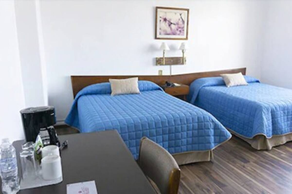 Quarto de hotel com duas camas, uma escrivaninha, um cesto de lixo e um quadro na parede.