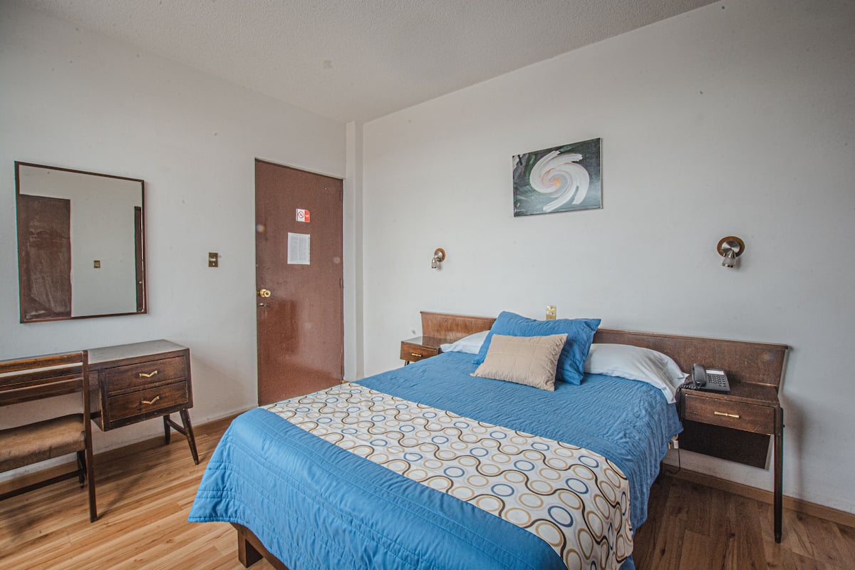 Um quarto com cama, mesas de cabeceira, escrivaninha e porta.