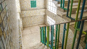 Uma escadaria em vários níveis, com guarda-corrimão verde e parede revestida de azulejos.