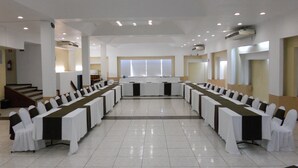 Uma sala de conferências com fileiras de mesas e cadeiras, uma escadaria e um aparelho de ar condicionado no teto.