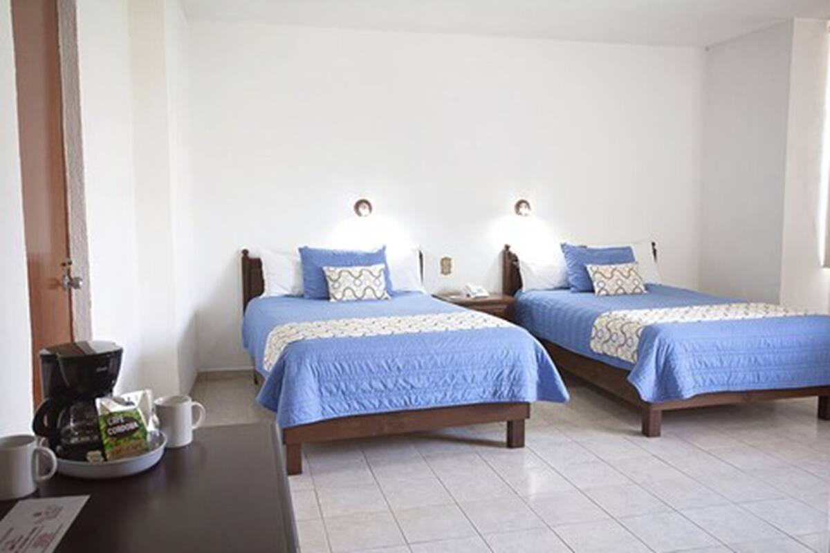Quarto de hotel com duas camas, uma cafeteira e um tabuleiro de café da manhã sobre uma mesa.