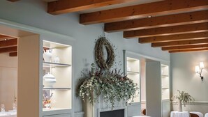 Um quarto espaçoso com vigas de madeira, lareira e um espaço de refeições com cadeiras e mesas.