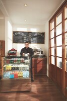 Um homem está atrás do balcão, com uma máquina de café e um quadro de cardápio em um café.