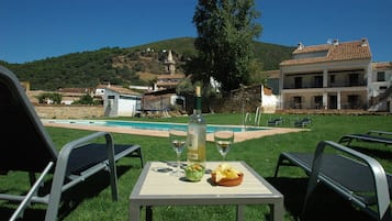 Mesa e cadeiras à beira da piscina, com uma garrafa e uma cesta de frutas.