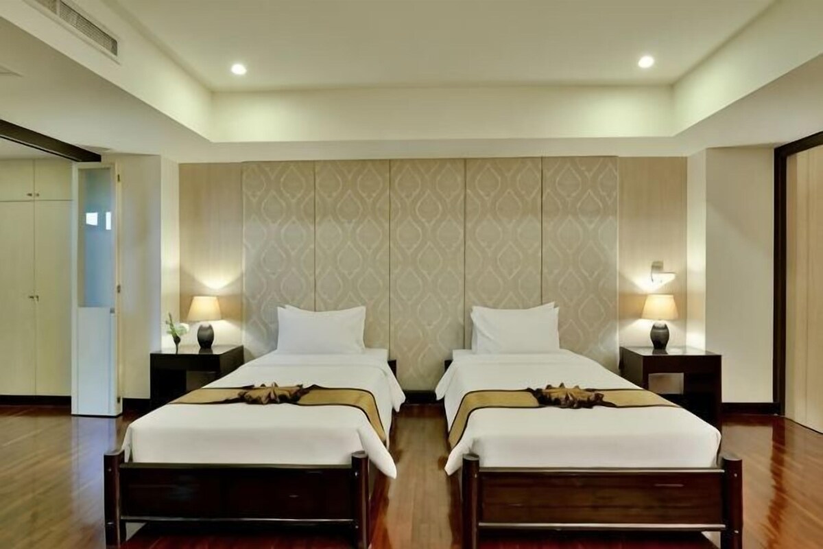 Quarto de hotel com duas camas, piso de madeira, parede estampada e abajures.