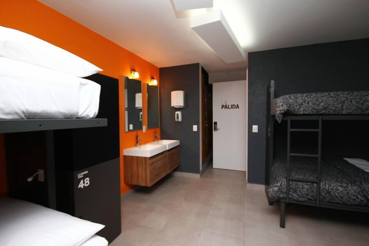 Quarto de hotel moderno com beliche, penteadeira com espelho e uma placa com a inscrição 'LA PÁLIDA'.