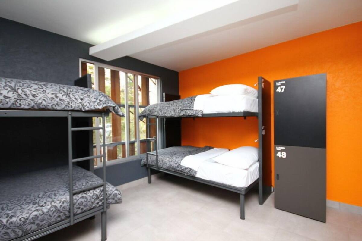 Quarto em dormitório com beliches, um guarda-roupa e janela com persianas.