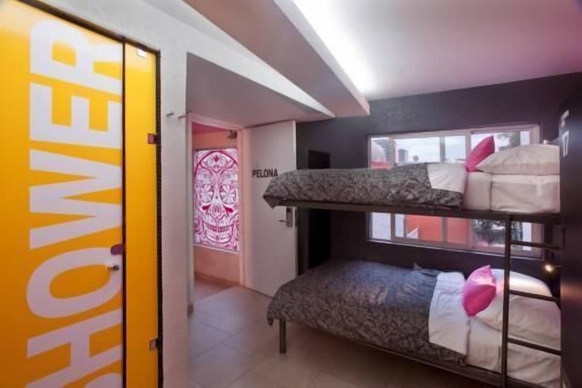 Quarto de hotel com beliches, área de chuveiro visível e janela com vista.