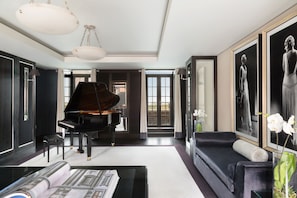 Uma sala de estar espaçosa com um piano de cauda, um sofá preto e um grande retrato emoldurado.