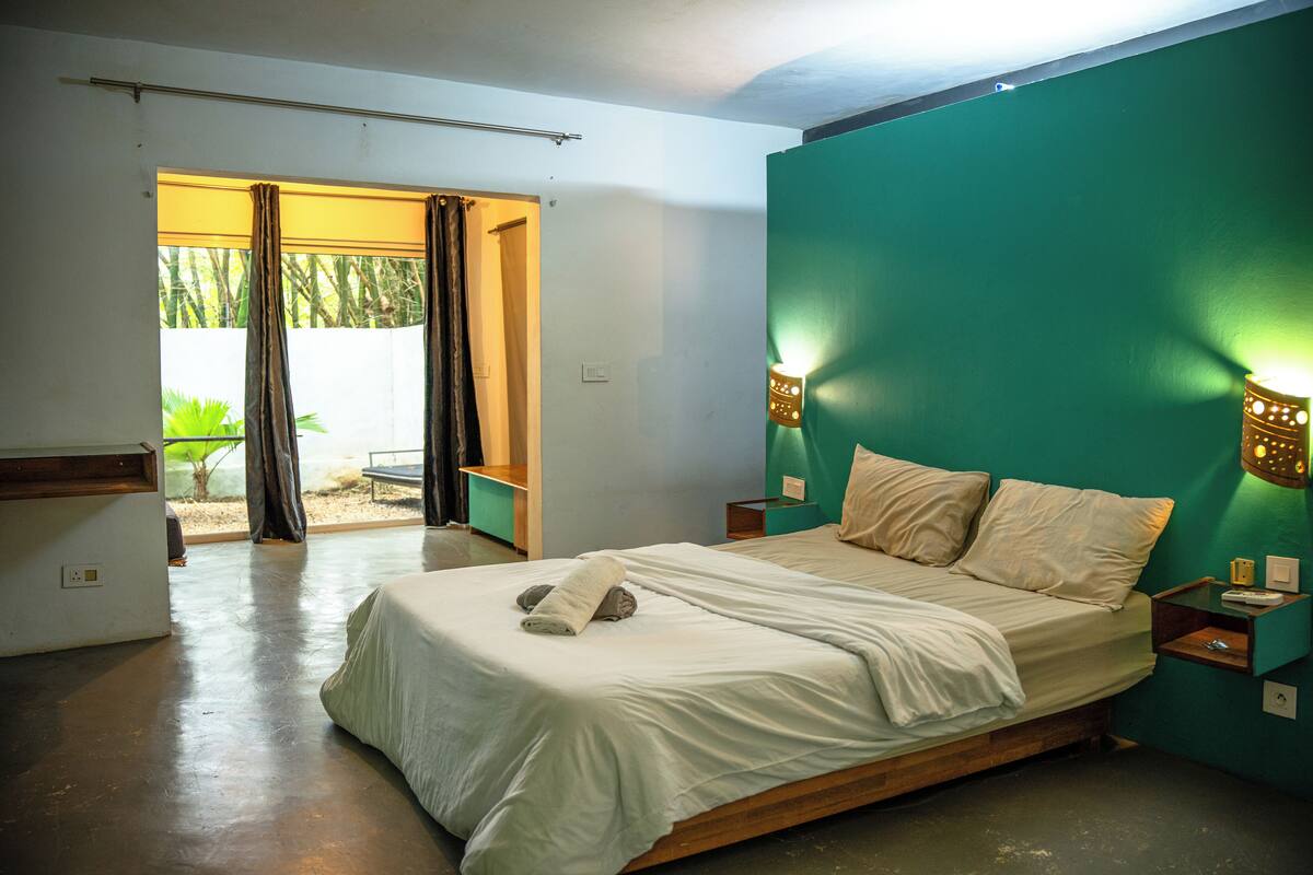 Quarto com cama, mesas de cabeceira e janela com cortinas.