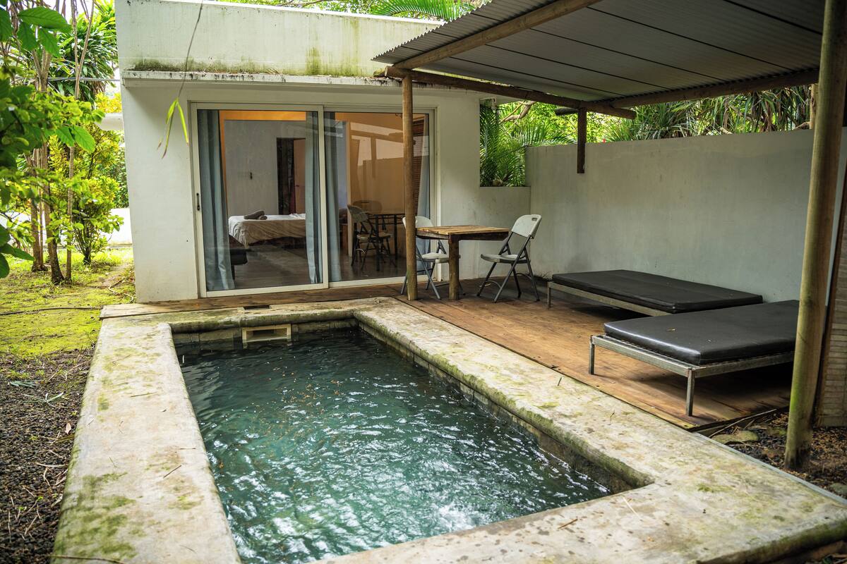 Uma área de piscina com uma piscina pequena, um deck de madeira e um espaço de estar coberto com uma mesa e cadeiras.