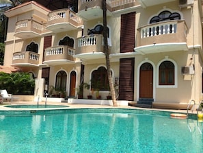 Um hotel com vários andares, varandas, piscina e um jardim tropical.