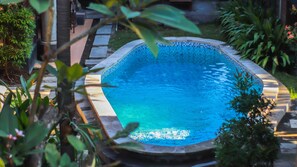 Piscina retangular com borda revestida em azulejo, ladeada por um caminho de pedra e vegetação exuberante.
