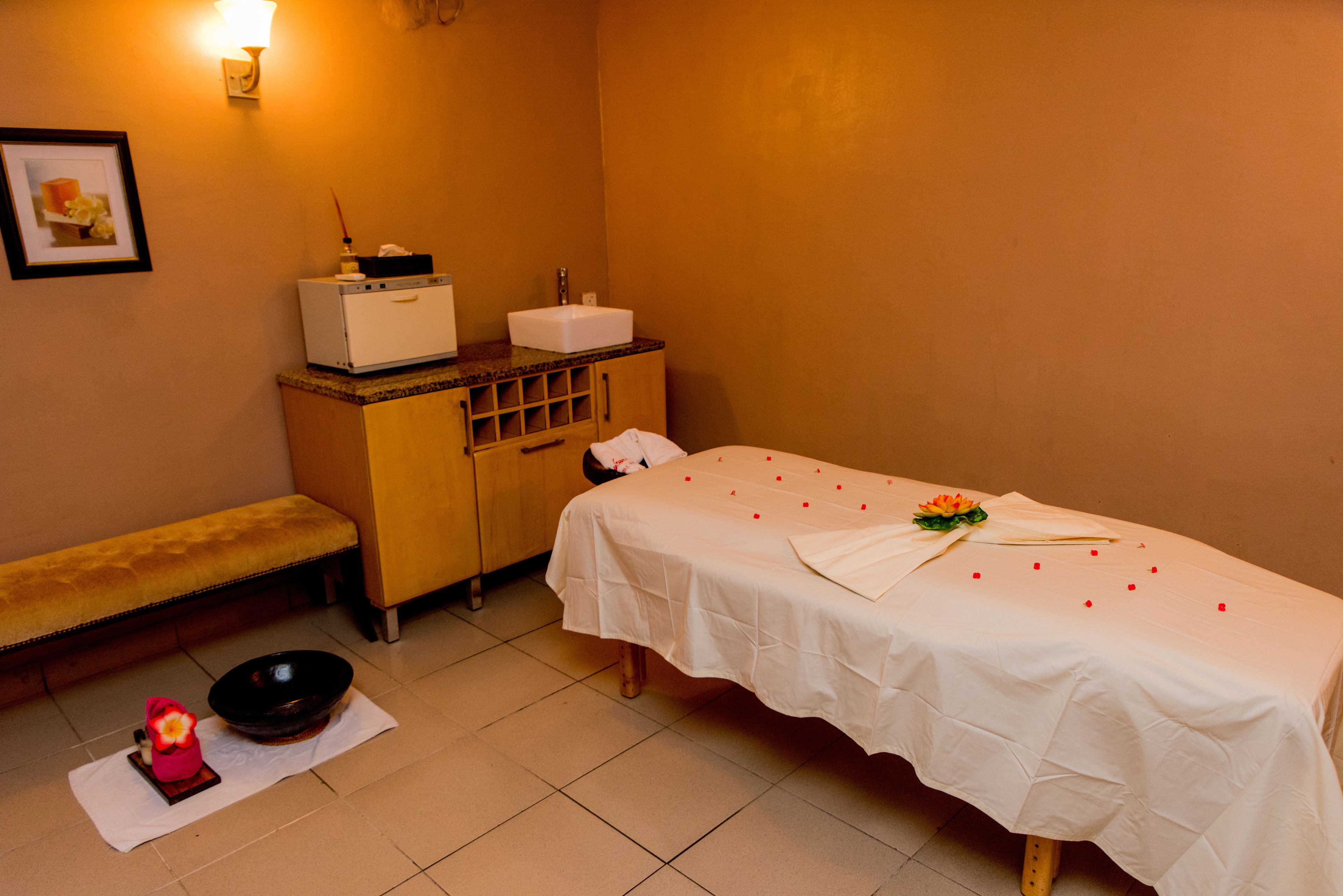 Um quarto com uma mesa de massagem, um pequeno armário, um banco e uma tigela.