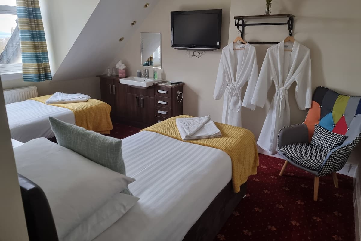 Quarto de hotel com duas camas, televisão, espelho, pia e uma cadeira com almofadas coloridas.