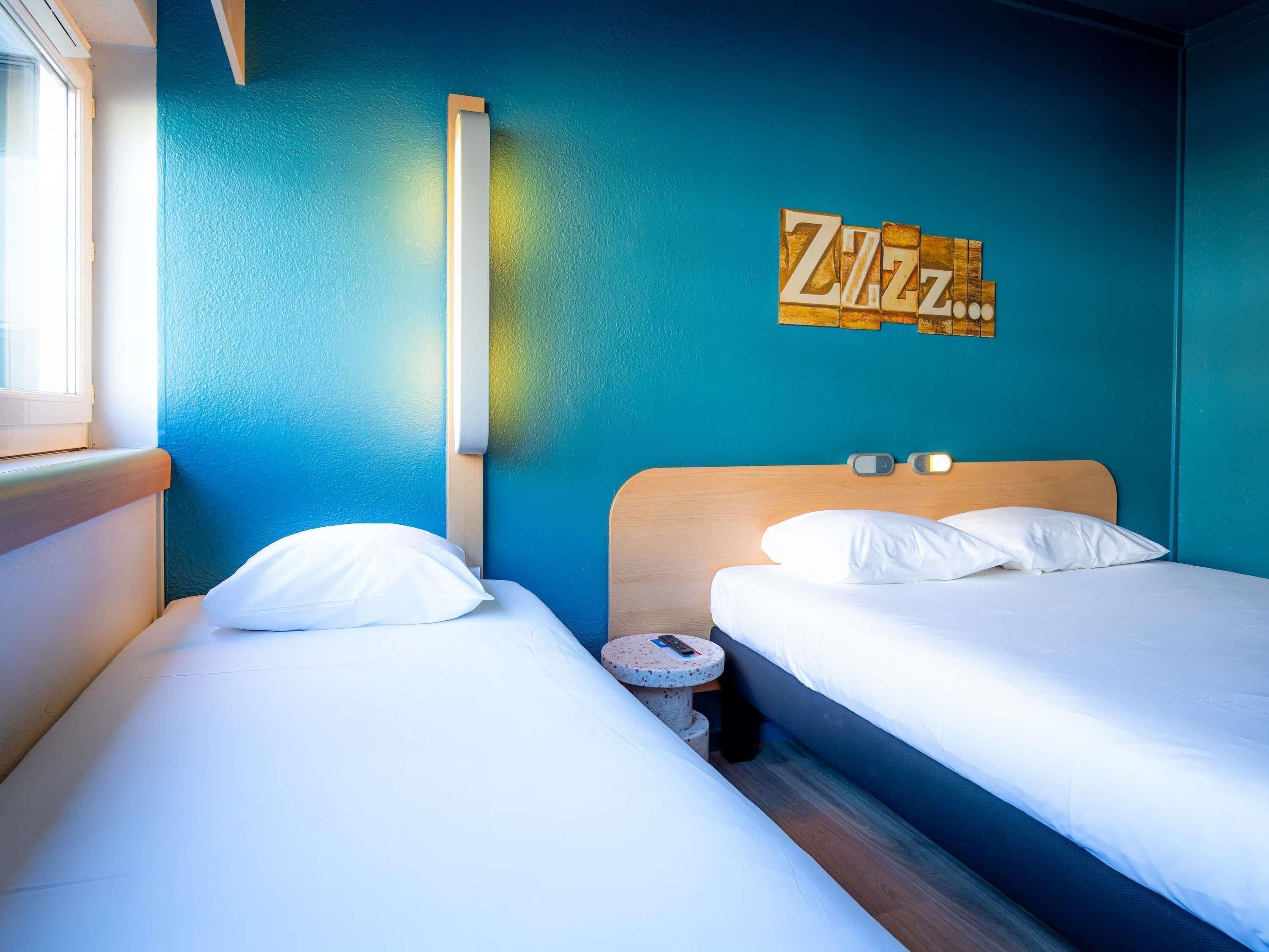 Quarto com duas camas, um relógio na parede e um letreiro 'Z.I.Z.Z'.