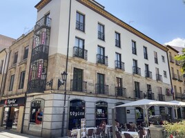 Um edifício com a placa 'Hostal', um restaurante 'Pizza Hut' e mesas ao ar livre com guarda-sóis.