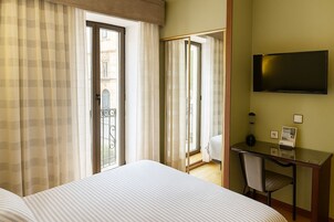 Quarto de hotel com uma cama, escrivaninha, televisão e vista para o exterior.
