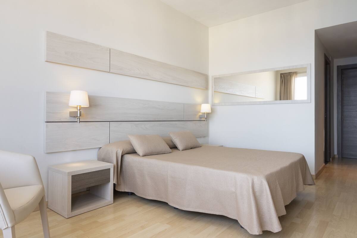 Quarto moderno com cama, mesas de cabeceira e iluminação embutida na parede.
