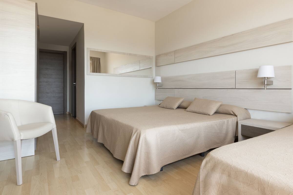 Quarto de hotel moderno com uma cama grande, uma cama menor, uma cadeira e uma mesa de cabeceira.