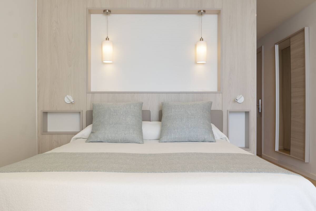 Quarto moderno com uma cama grande, duas mesas de cabeceira e um aplique na parede.