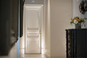 Um corredor com uma porta branca fechada, um aparador de madeira escura com gavetas e um vaso de flores em cima.