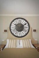 Uma cama com um relógio de parede grande, duas mesas de cabeceira e almofadas listradas.