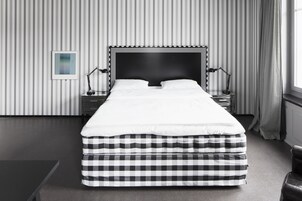 Cama bem arrumada com saia de cama quadricula preta e branca, cabeceira preta e duas luminárias de cabeceira.