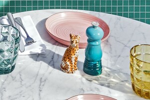 Uma mesa de mármore com um prato rosa, um saleiro e pimenteiro azuis, um saleiro com estampa de leopardo, um copo e um garfo.