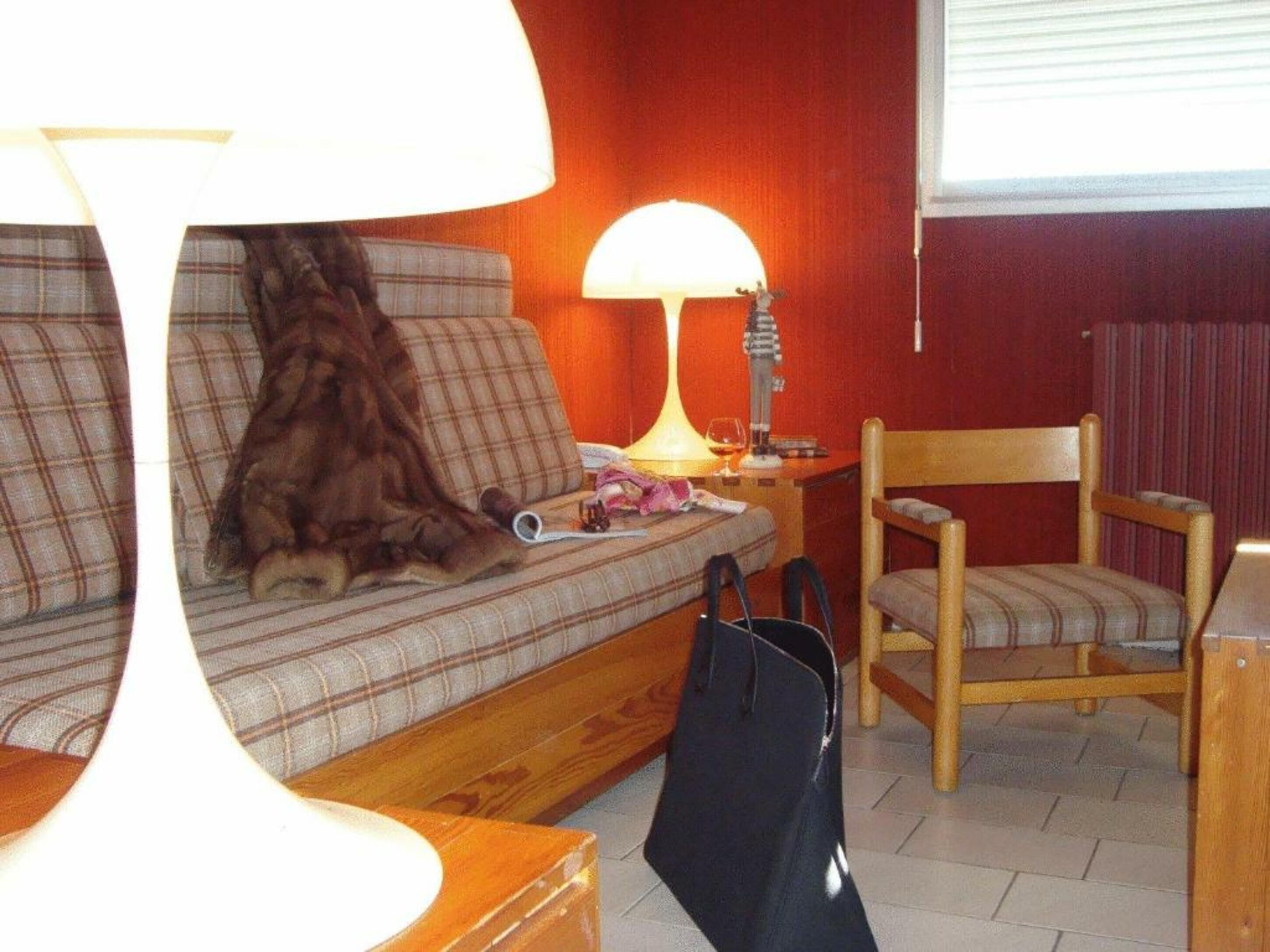 Uma sala de estar aconchegante com um sofá xadrez, uma cadeira de madeira, um abajur e uma bolsa preta no chão.