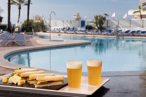 Área de piscina com espreguiçadeiras, piscina e uma bandeja com sanduíches e duas cervejas.