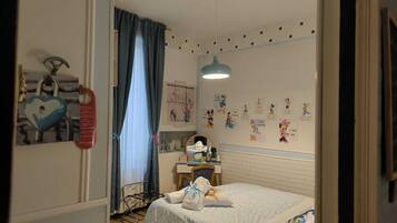 Quarto com cama, escrivaninha e cadeira. Cortinas, relógio de parede e cartazes motivacionais.