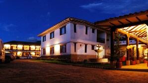 Um edifício de dois andares com telhado em telhas, uma área externa coberta com assentos e uma fonte em frente.