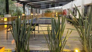 Um espaço interno com mesa de pingue-pongue, plantas em vasos e teto de vidro.
