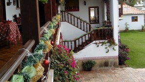 Uma casa com escadaria de madeira que dá para uma varanda, cercada por vegetação e vasos de plantas.