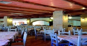 Restaurante com várias mesas e cadeiras, pilares de pedra e teto de madeira.
