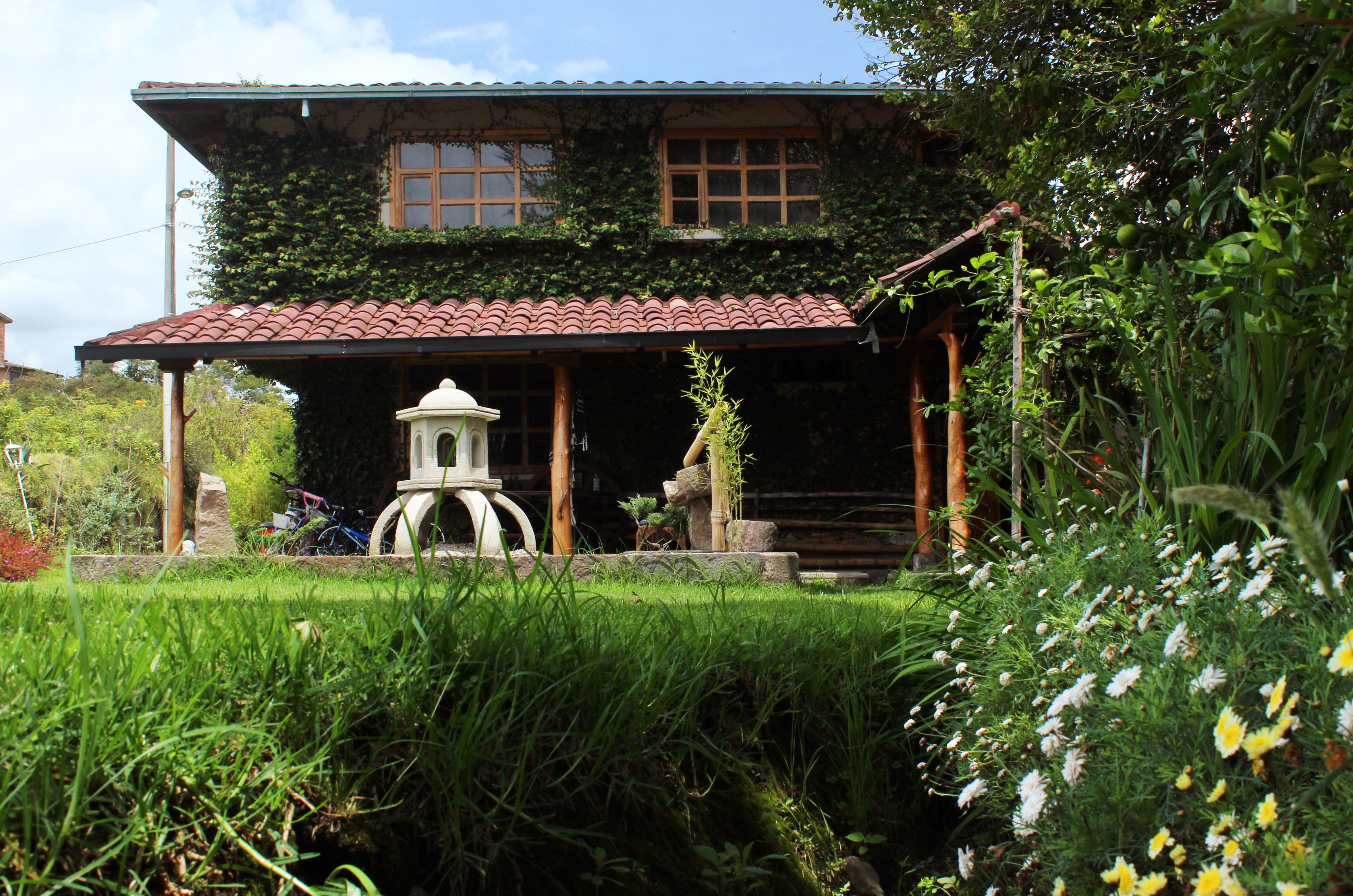 Uma casa rústica com telhado de telhas vermelhas, chaminé de pedra e um pequeno candeeiro branco na frente.