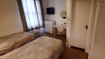 Quarto de hotel com duas camas, uma escrivaninha, uma cadeira, uma televisão e uma porta.
