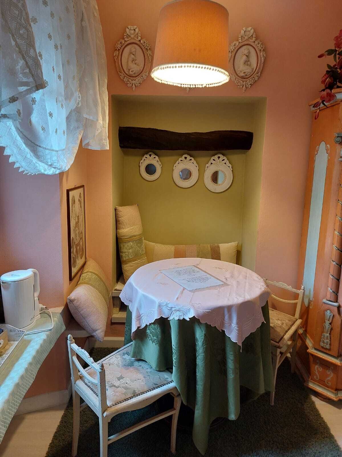 Quarto aconchegante com uma mesa redonda, uma cadeira, um abajur e um espelho na parede.