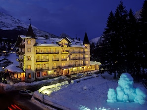 Um hotel grande e com vários andares, com telhados cobertos de neve e uma torre imponente.