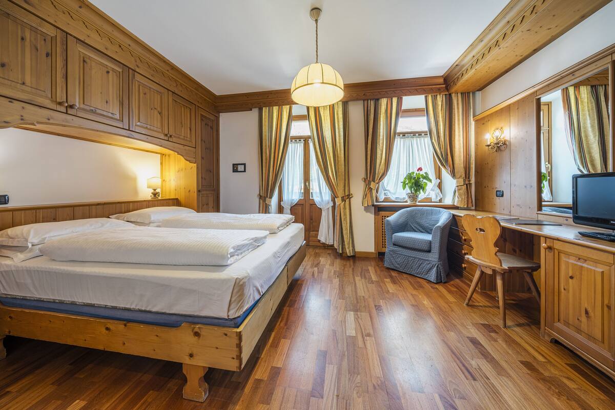 Quarto com cama de madeira, escrivaninha com computador e uma cadeira.