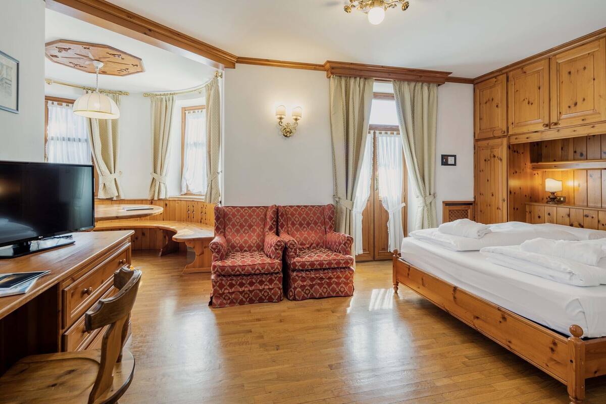 Um quarto acolhedor com uma cama de madeira, televisão, uma cadeira vermelha com padrão e armários de madeira.