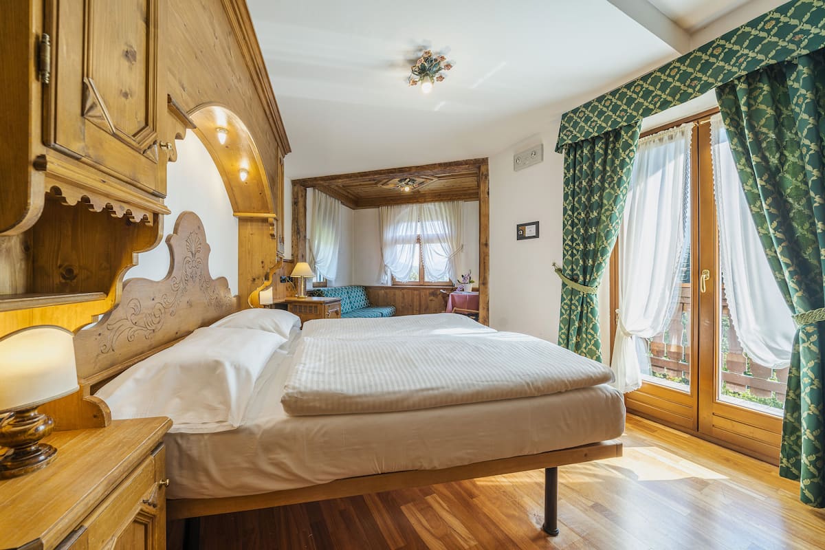 Quarto com estrutura de madeira, cama, mesa de cabeceira e janela com cortinas.