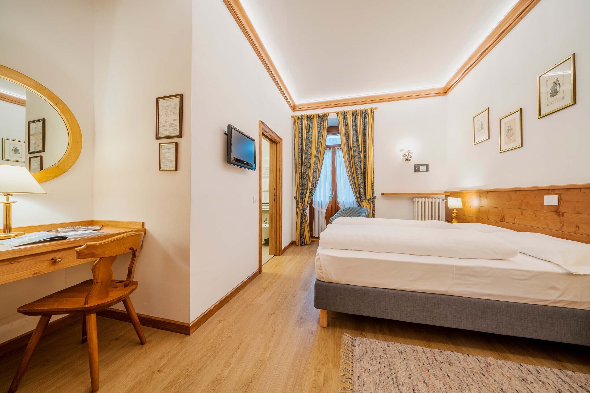 Quarto de hotel com uma mesa de madeira, uma cama, uma televisão e quadros nas paredes.