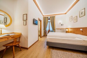 Quarto de hotel com uma mesa de madeira, uma cama, uma televisão e quadros nas paredes.