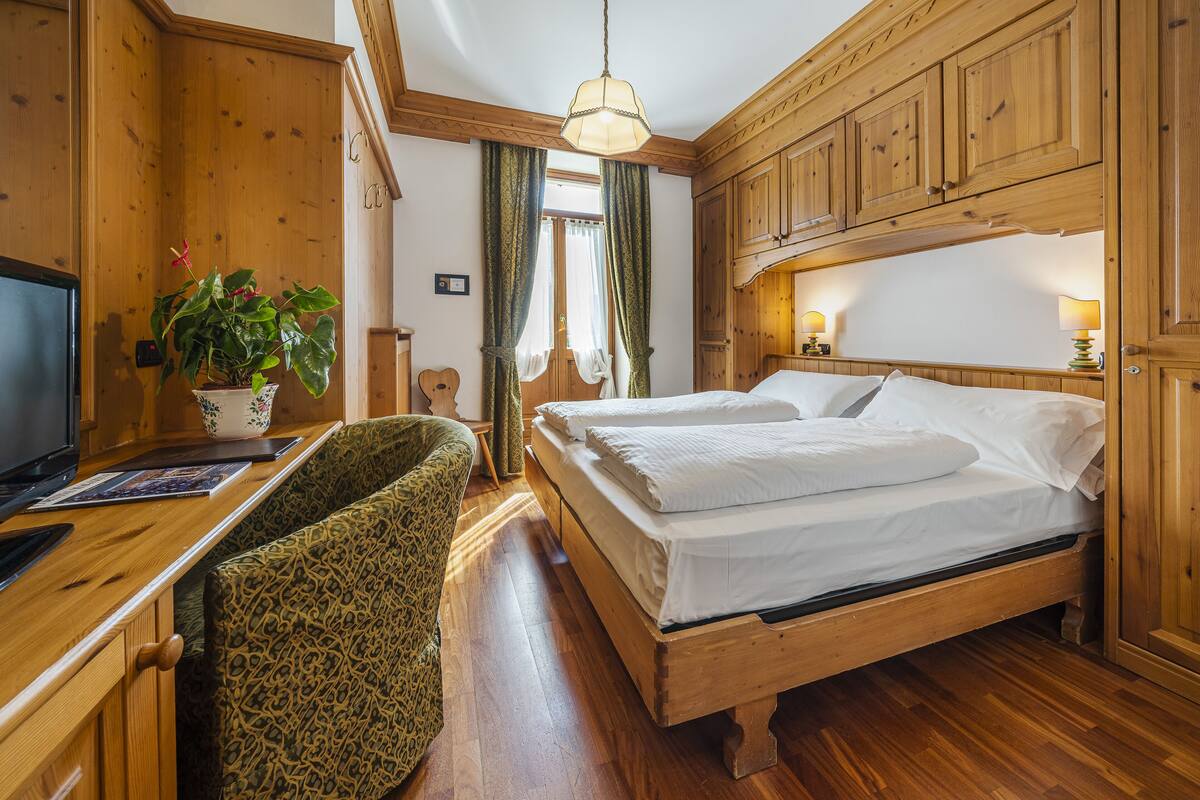 Quarto de madeira com uma cama, uma escrivaninha, uma cadeira e um vaso de planta.
