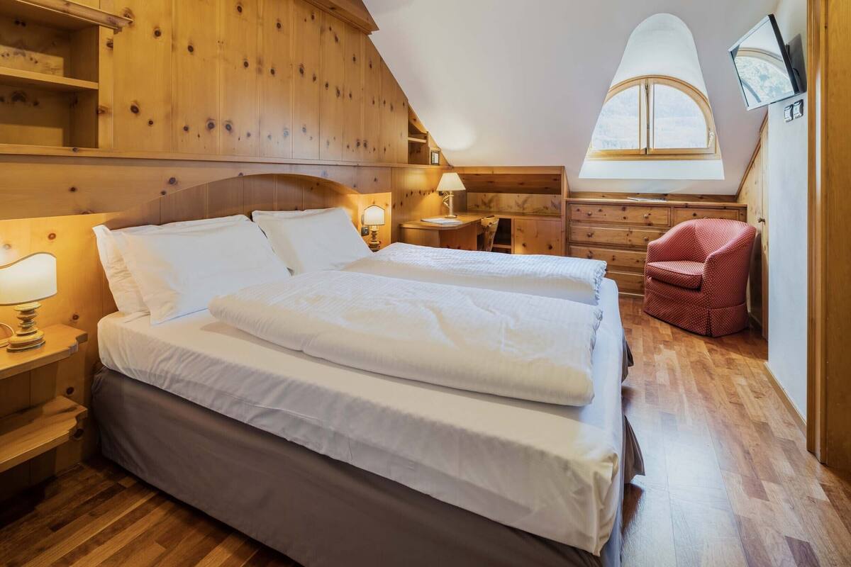 Quarto com duas camas, paredes de madeira, escrivaninha, cadeira e janela.