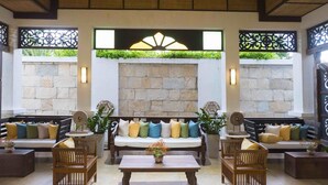 Uma área de estar ampla e coberta, com parede de pedra, móveis de madeira e detalhes decorativos.